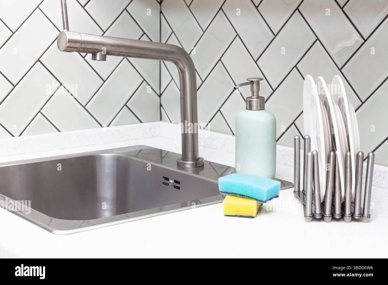 Stainless steel sink with clean plates in dish rack, soap bottle, and ...