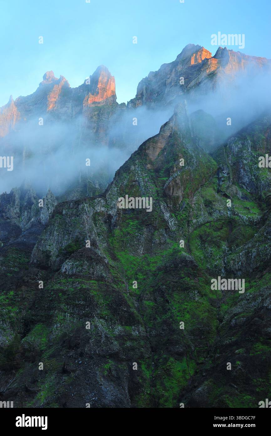 Tall mountain peaks of Madeira catching sunset light above the clouds ...