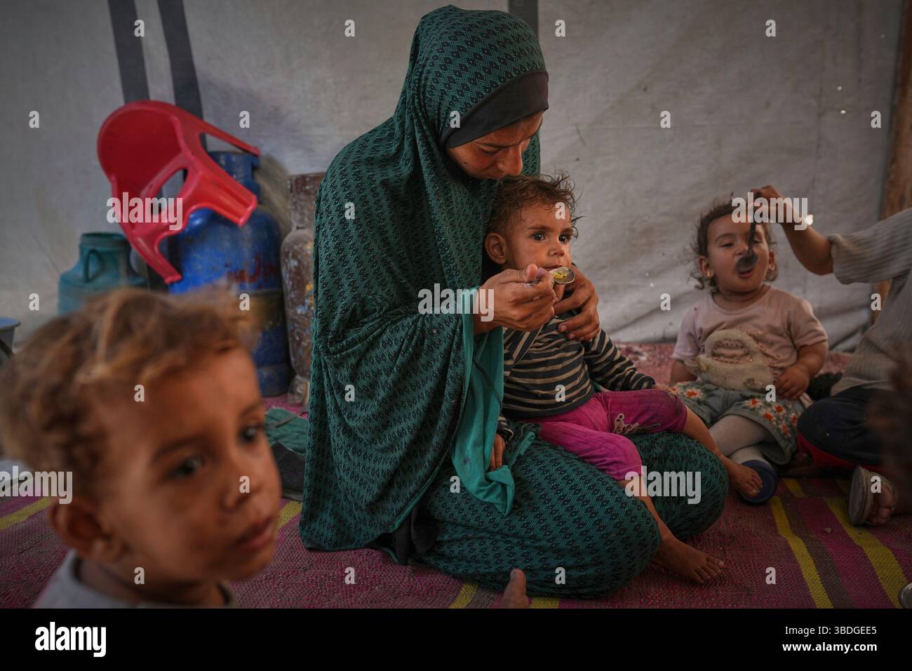 A Palestinian woman feeds her children at a tent sheltering a displaced ...