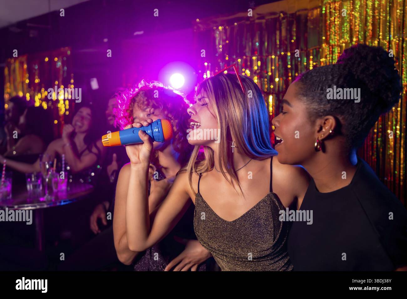 Young women enjoying karaoke night, singing with microphone and having ...