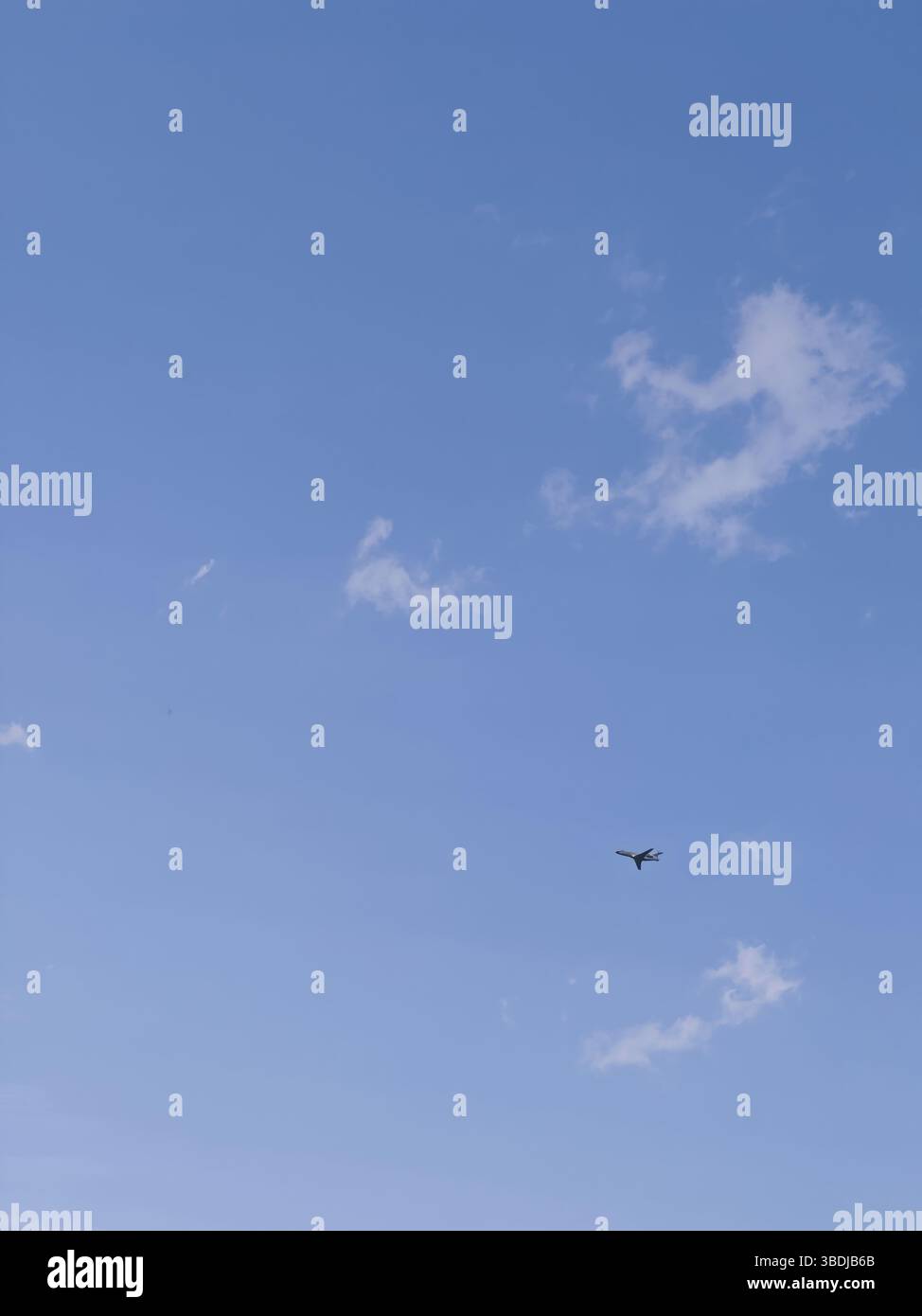 Jet airplane flying high in a bright blue sky with scattered thin ...