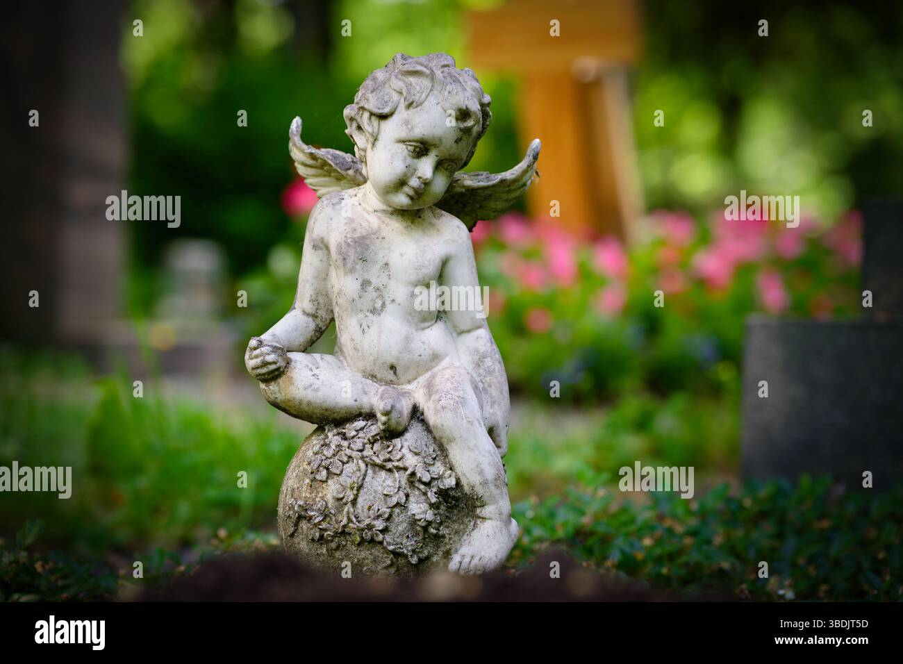 a small, slightly weathered putto sits on an ornate sphere on a grave ...