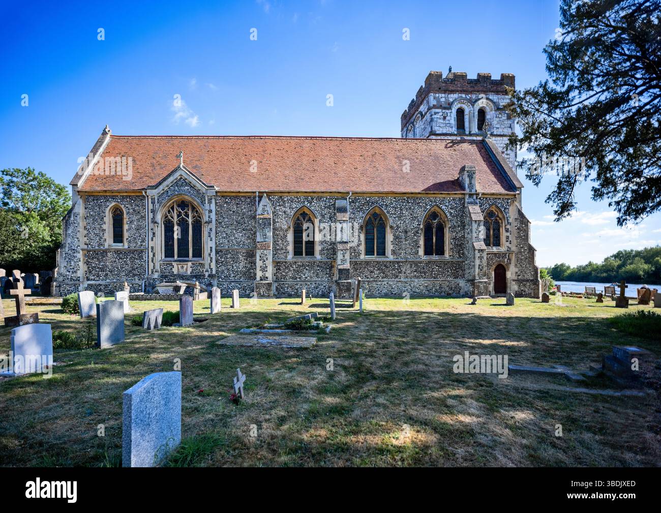 Side elevation of a long, historic flint church with a red tiled roof ...