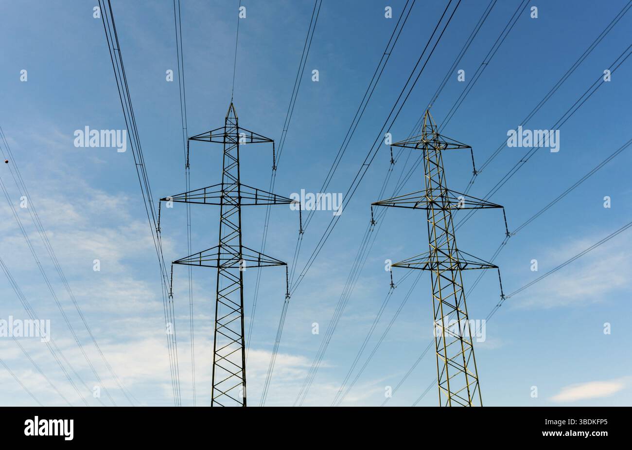 high voltage power lines and lattice crosses under a blue sky with ...