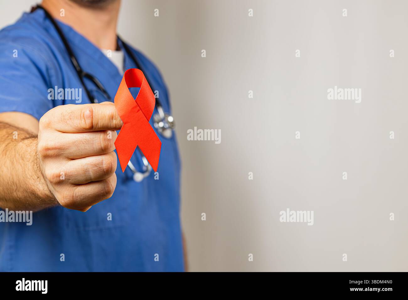 A healthcare worker in scrubs displays a red ribbon, symbolizing ...