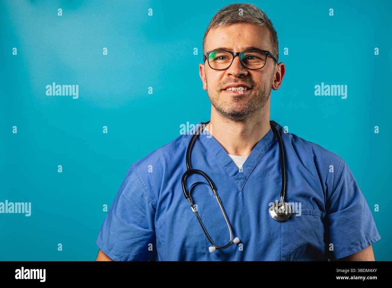A smiling healthcare professional wears blue scrubs and glasses ...