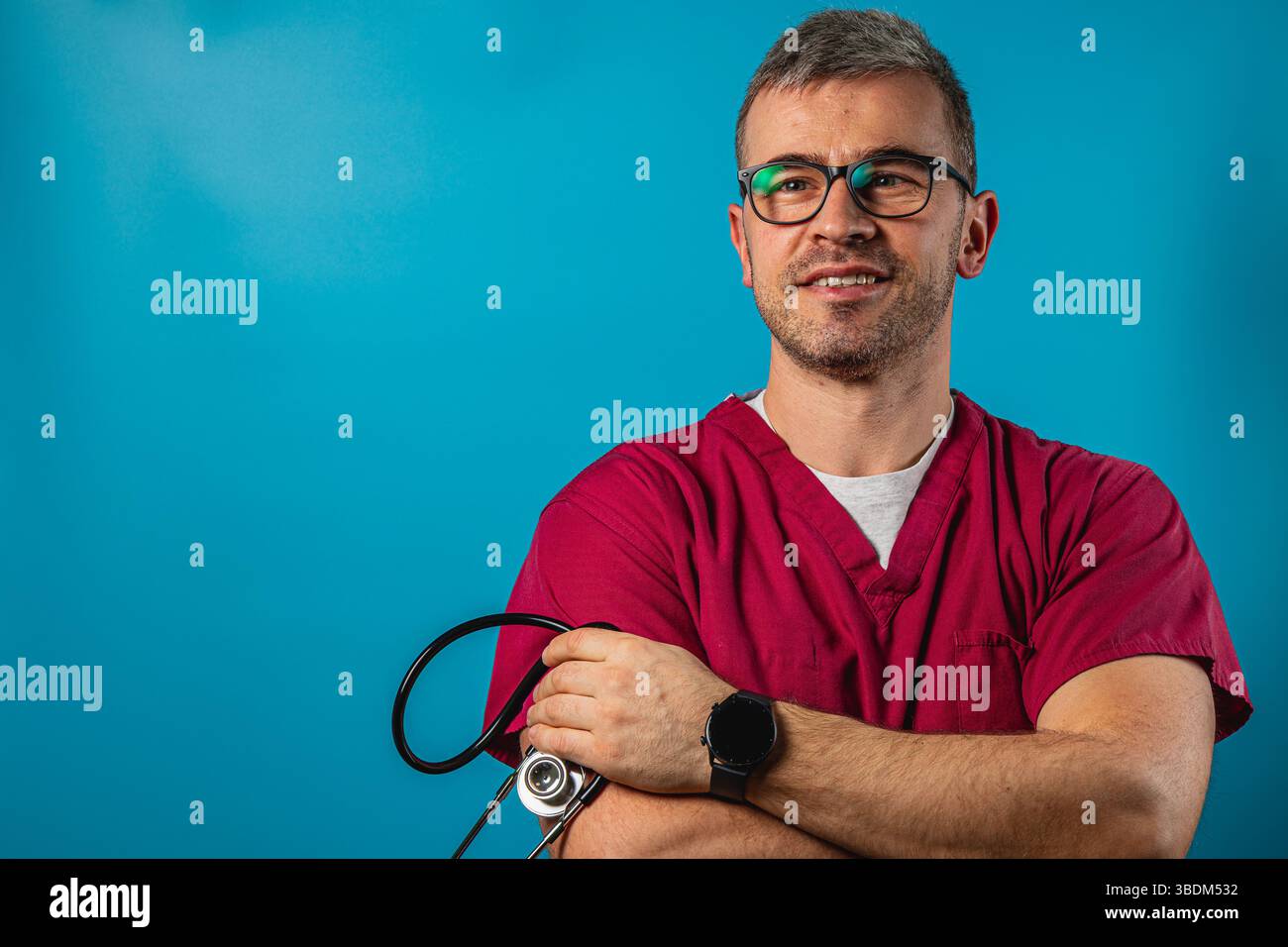 A smiling healthcare professional wearing pink scrubs and glasses poses ...