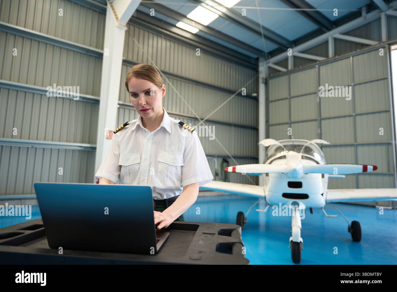 Female pilot using laptop in aircraft hangar with small plane Stock ...