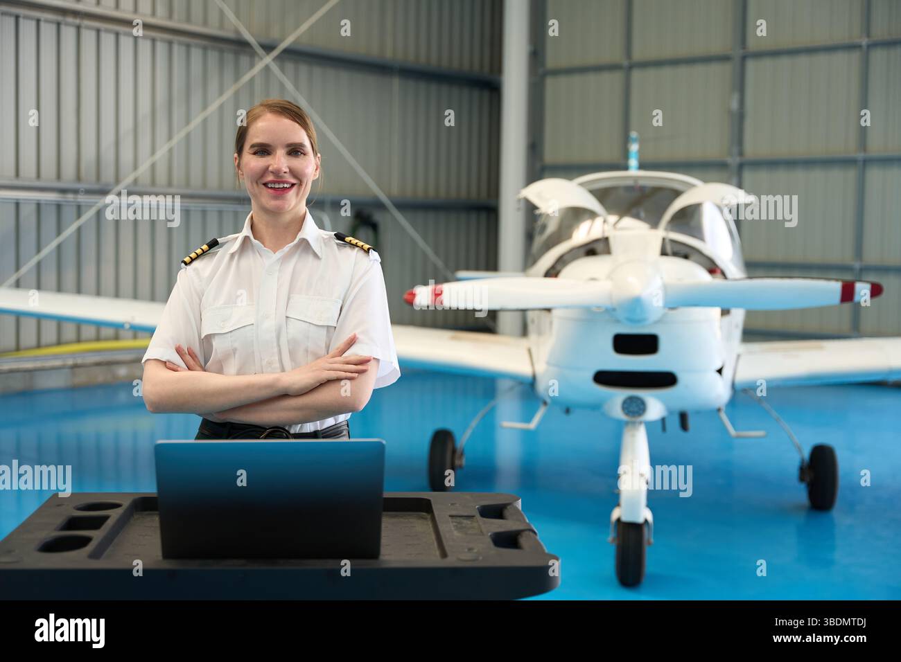 Confident female pilot posing in aircraft hangar with laptop Stock ...