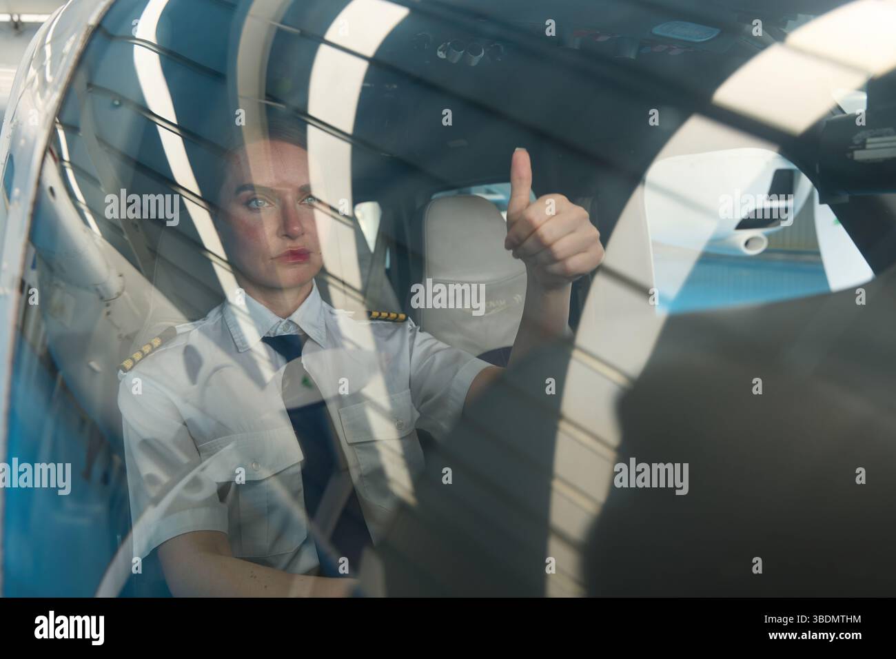 Confident female pilot gesturing thumbs up inside aircraft cockpit ...