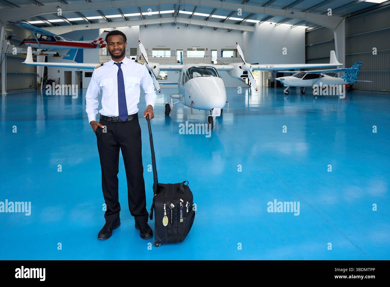 Airline pilot posing in hangar with suitcase and airplanes Stock Photo ...