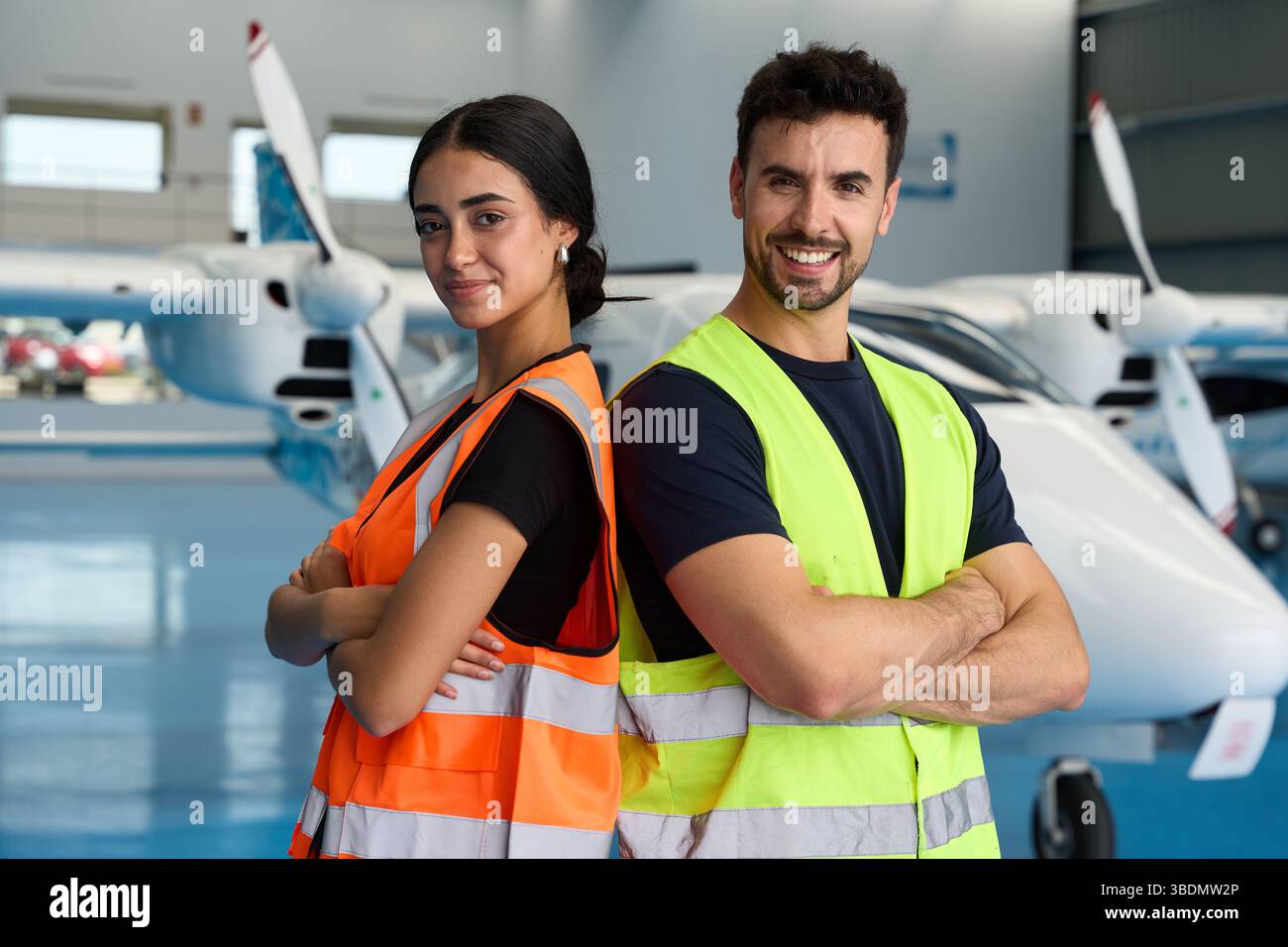 Aircraft mechanics smiling with arms crossed in hangar with airplanes ...