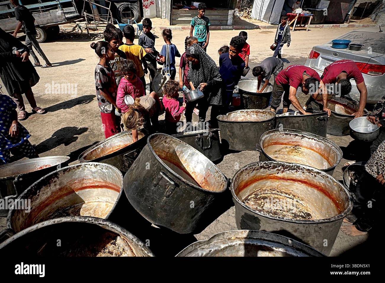 Palestinians wait in long queues to receive pots of food distributed by ...