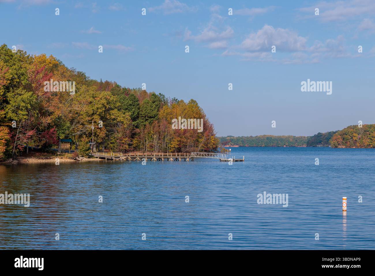 Floating dock in front of bright colorful fall foliage along the shore ...