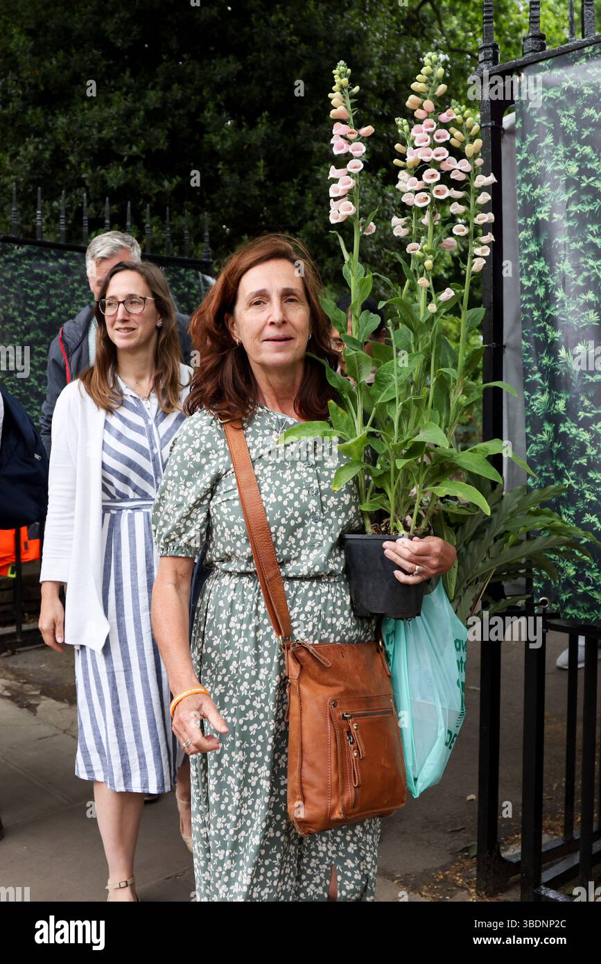 A woman carrying a pot of flowers departs from the RHS Chelsea Flower ...