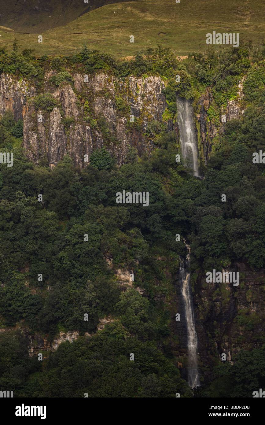 Tall waterfall cutting through dense green woodland and rocky cliffs on ...