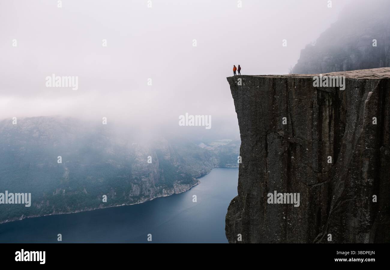 Two adventurers stand atop a towering cliff in Preikestolen Norway ...