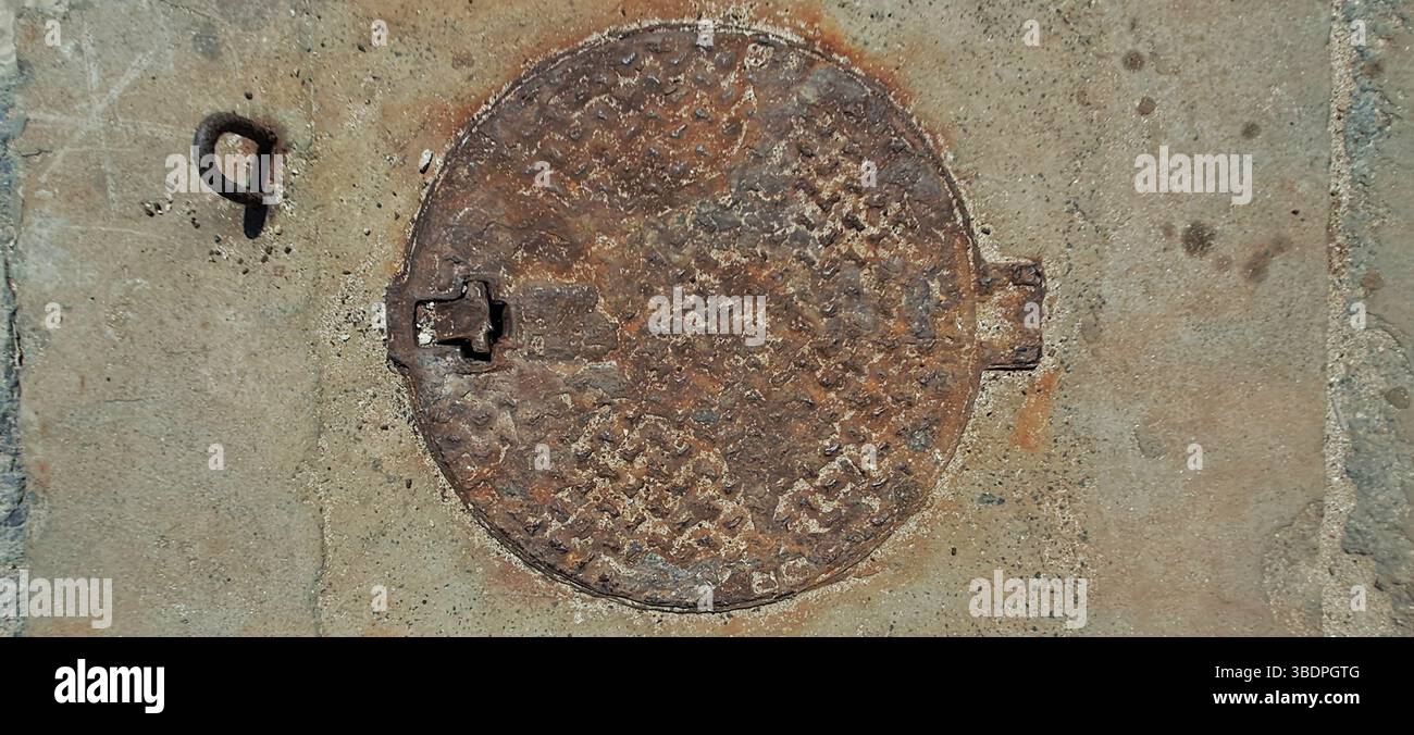 Rusty round manhole cover closed and embedded in the concrete ground ...