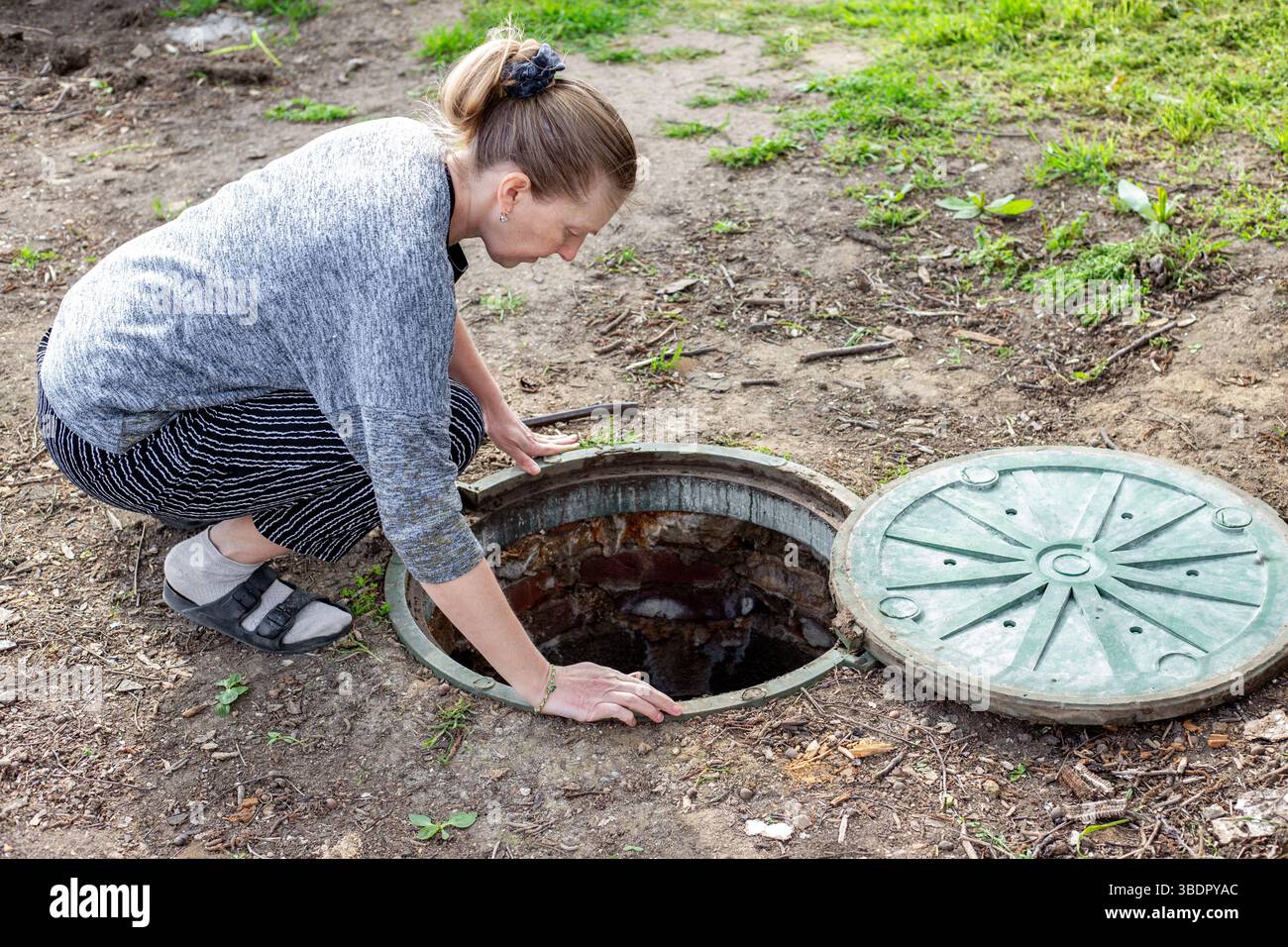 A woman looks into an open septic tank to check the level of sewer ...