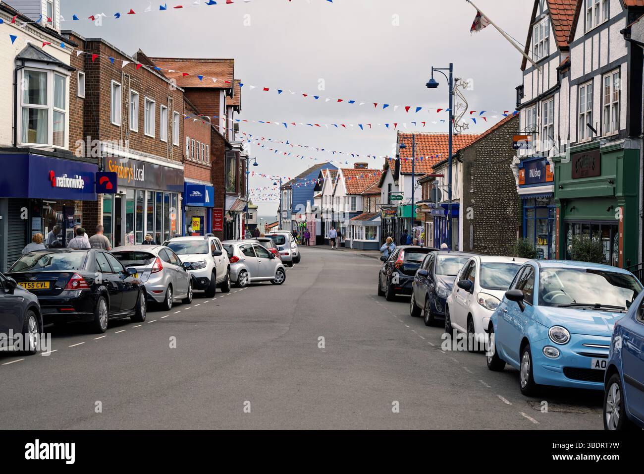 Shoppers and parked cars along the High Street in Sheringham, Norfolk ...
