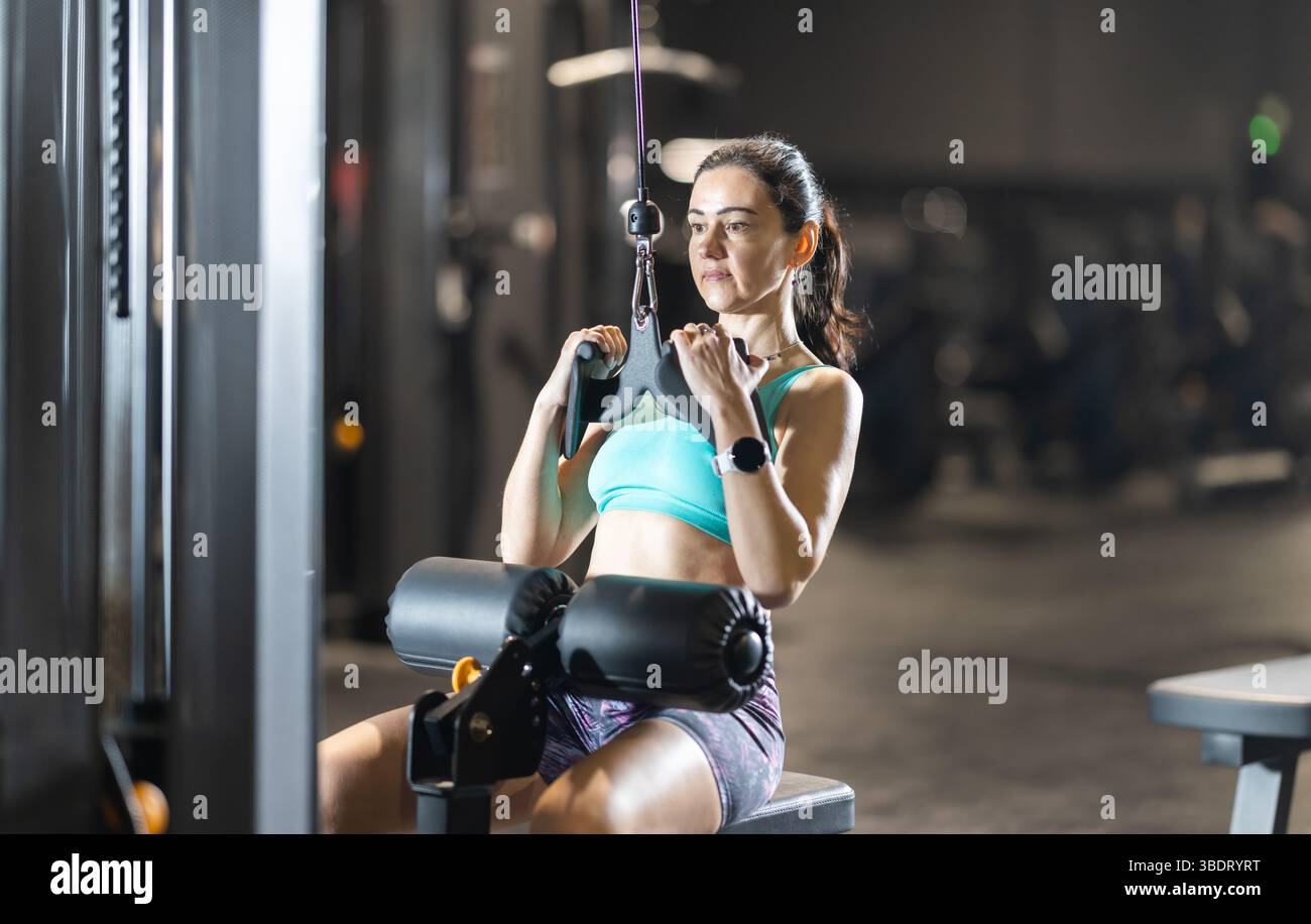 Fit woman performing lat pulldown on cable machine at gym Stock Photo - Alamy