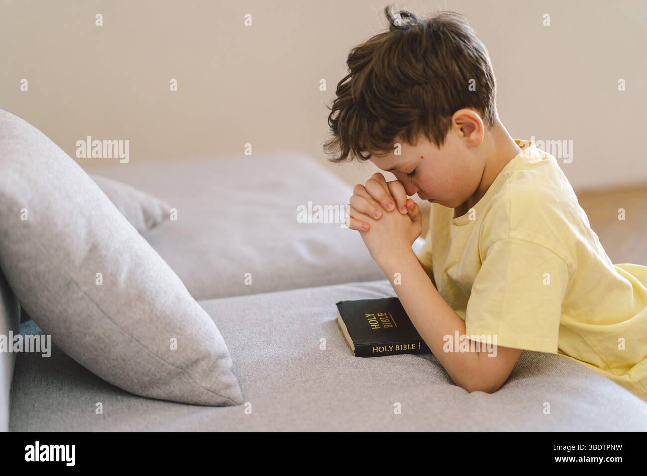 A boy with folded hands in front of him, he prays in his room Stock ...