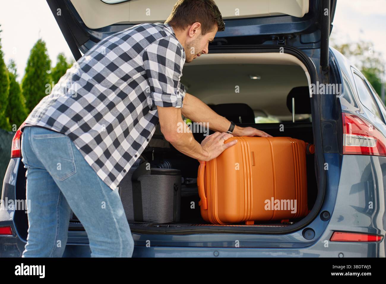Man loading orange suitcase into car trunk before journey. Packing ...