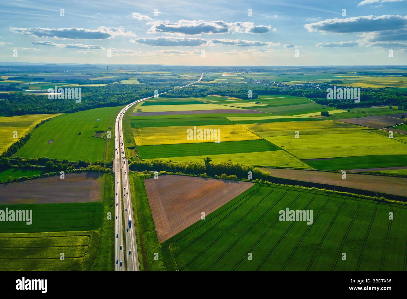 Aerial view of highway cutting through agricultural fields with blooming rapeseed crops ...