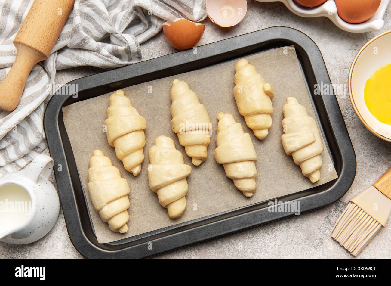 Raw croissants on baking sheet, ready for the oven, with ingredients and tools around Stock ...