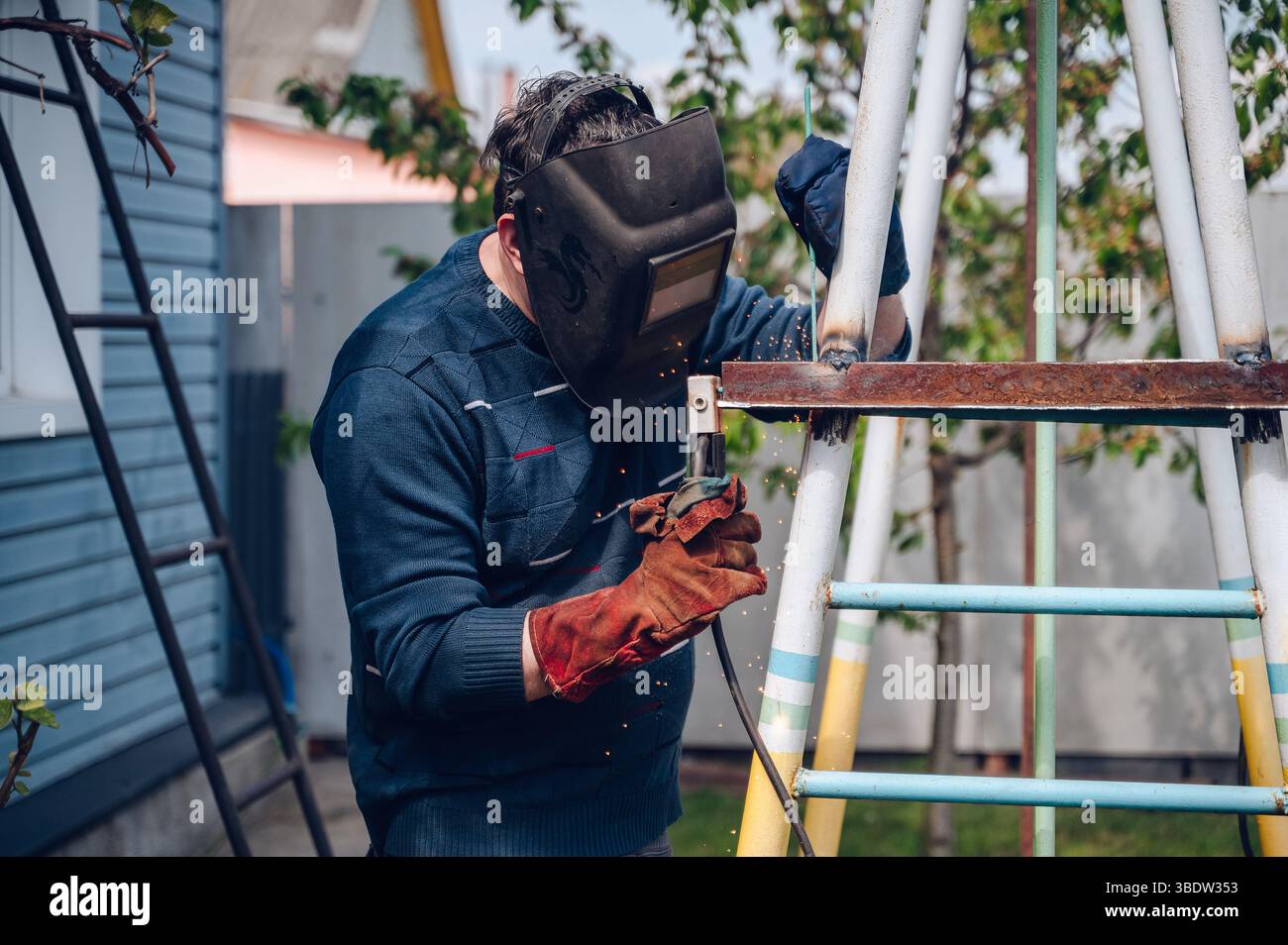 A male welder in a welding mask welds metal with a welding machine on a ...