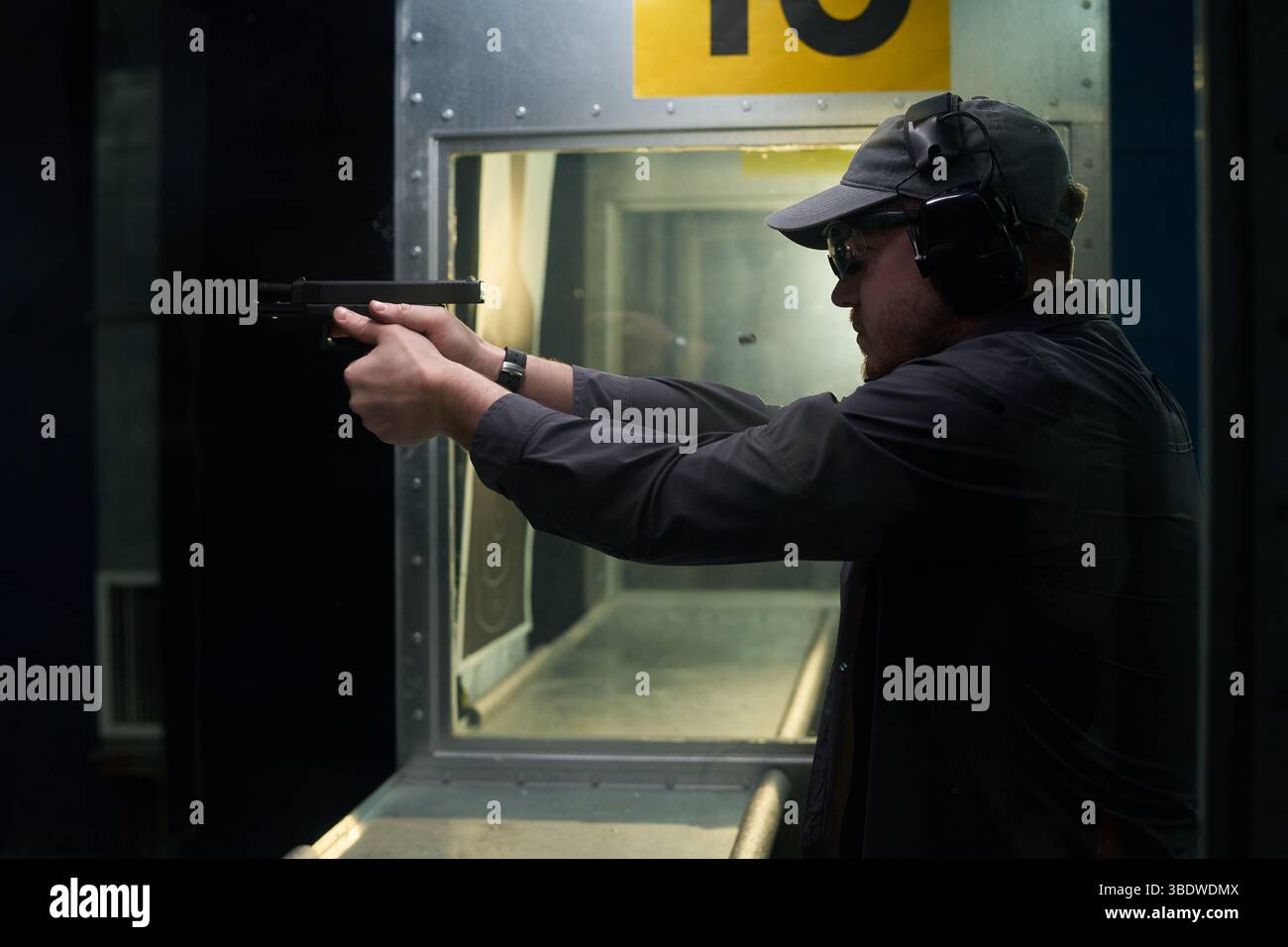 Man in protective gear practicing shooting at indoor range with handgun ...