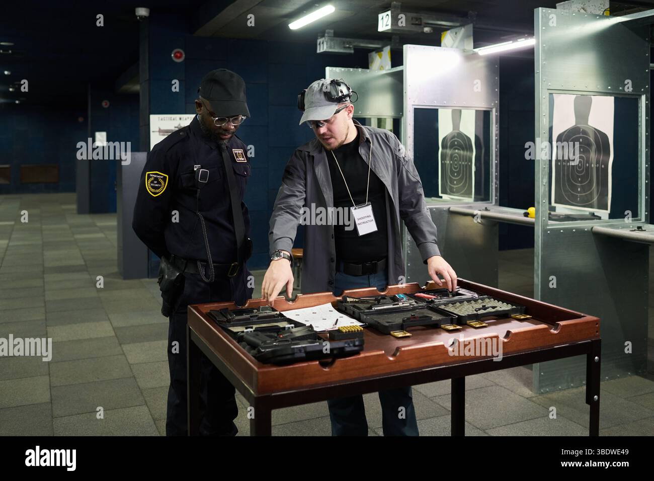 Two men examining various firearms at shooting range, one in security uniform and other in ...