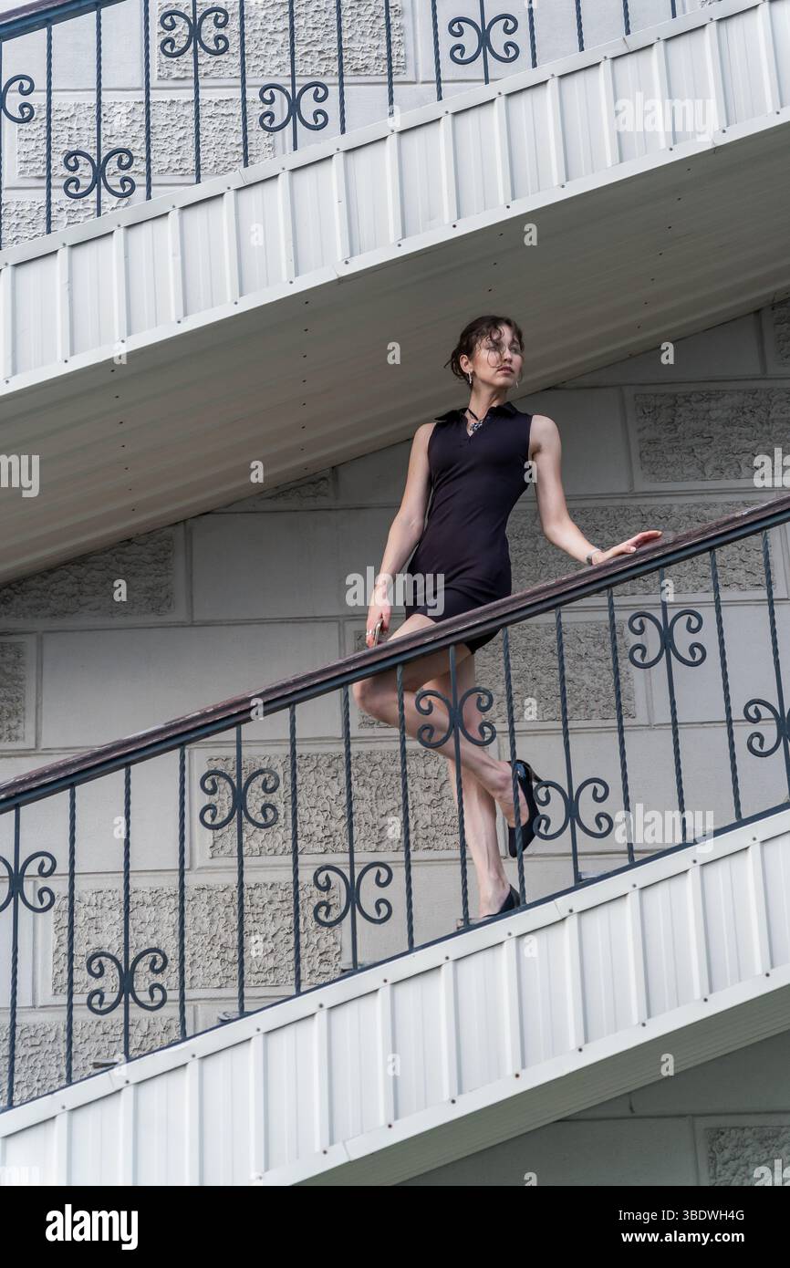 A woman in a black dress poses on a staircase with decorative railings ...