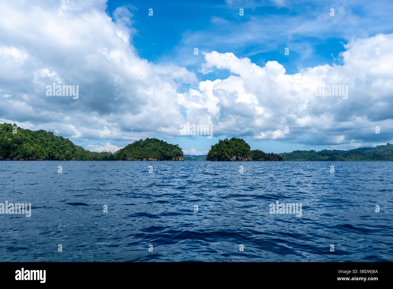 Small forested islets rise from the deep blue water under a sky filled ...
