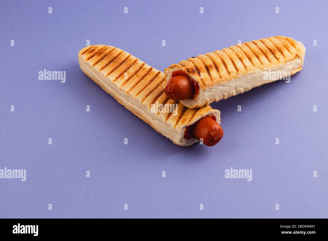 Two uniquely shaped grilled hot dogs sit on a purple background ...