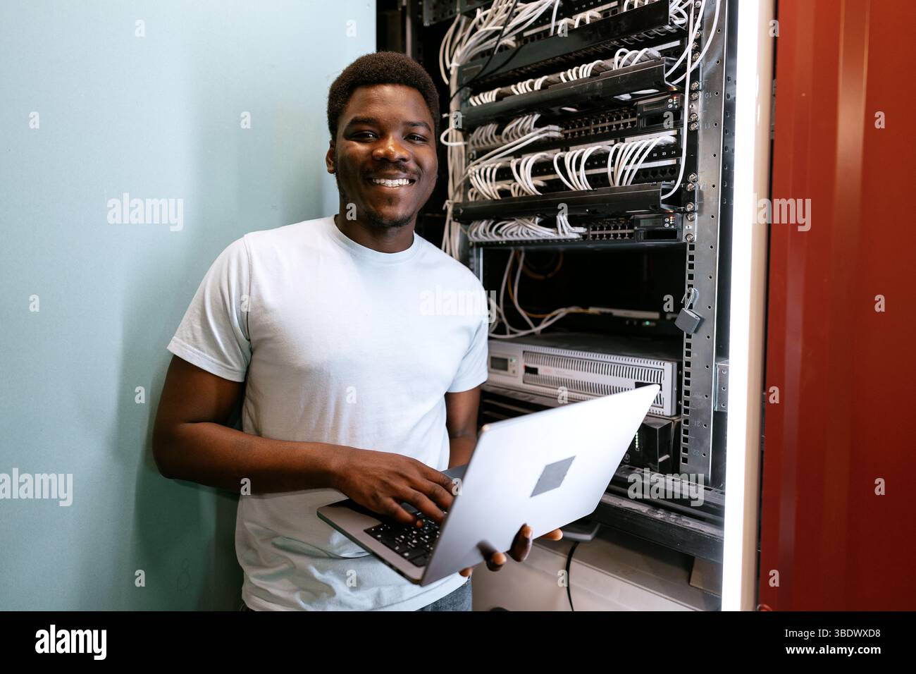 Young professional managing servers with laptop while smiling in a data ...