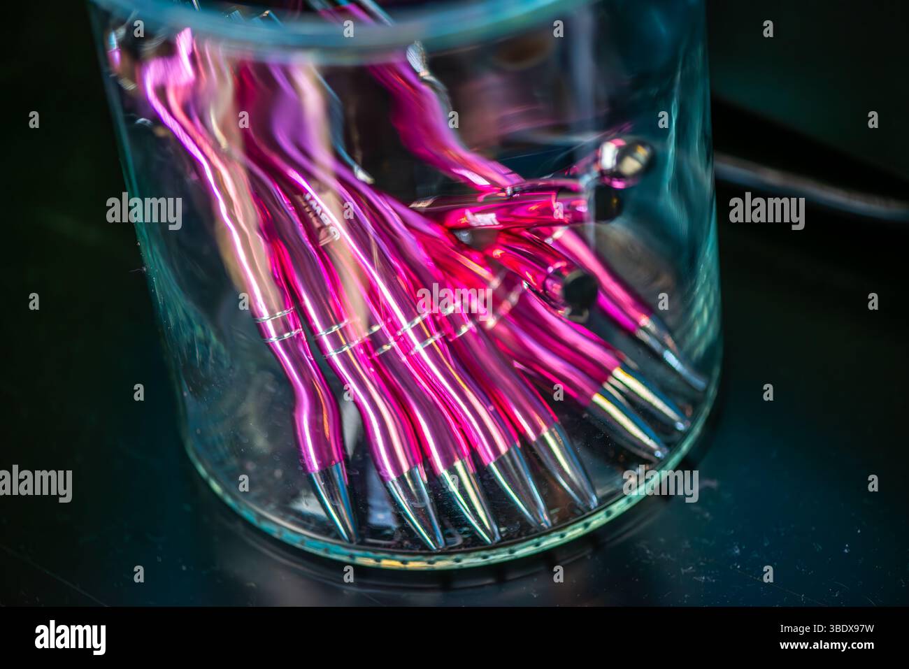 A neatly arranged set of pink pens displayed inside a transparent glass ...