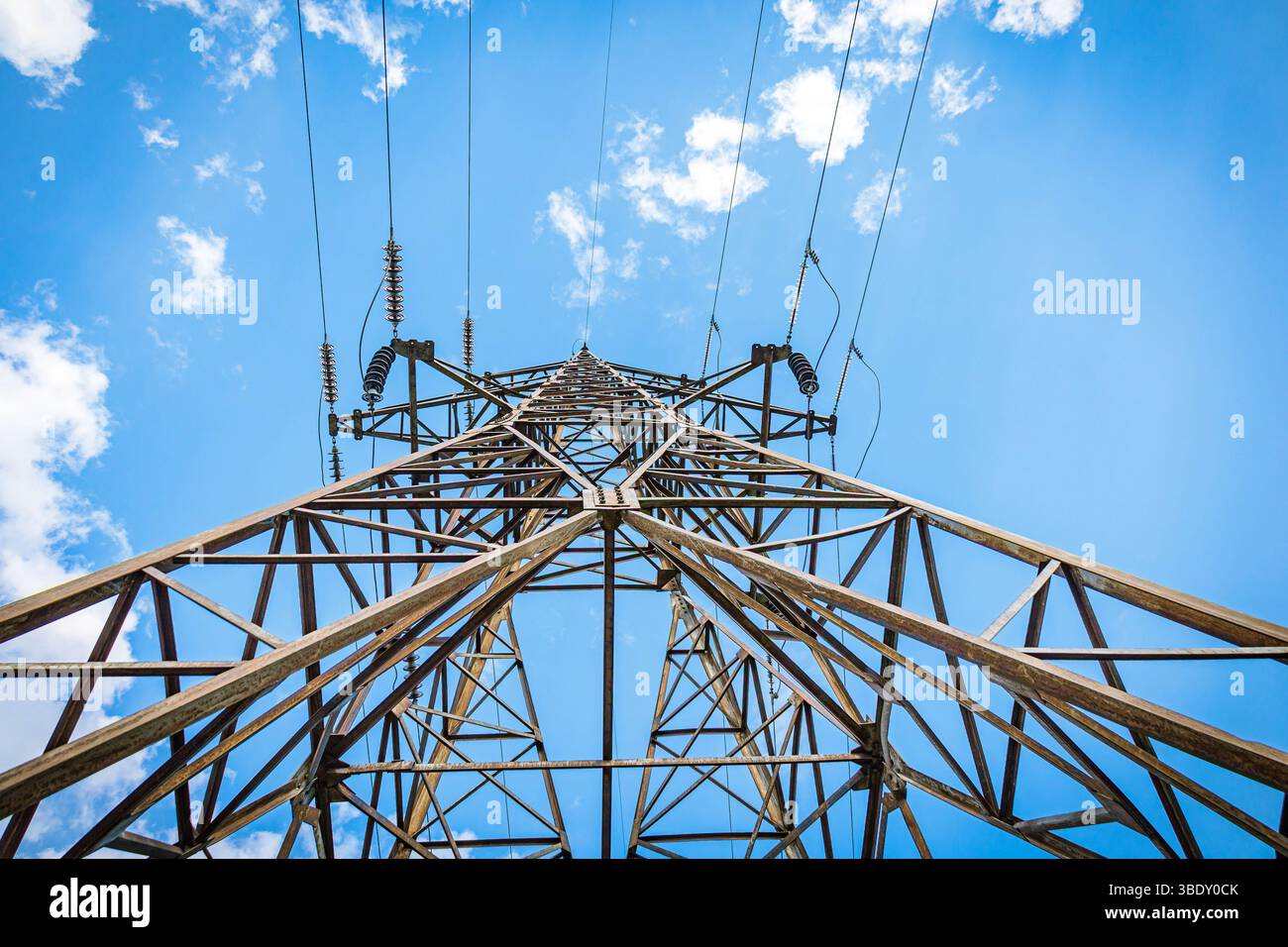 Electricity transmission tower photographed from below with high-voltage lines against a clear ...