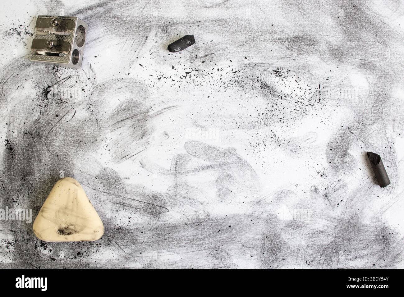 Black dust and smudges on white paper next to an eraser and a sharpener ...