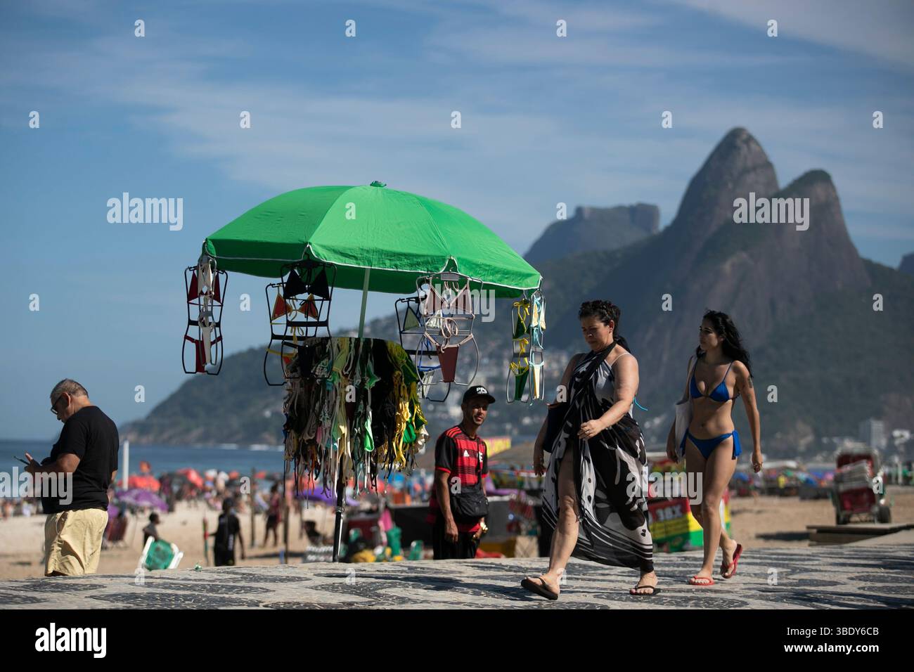 Beachgoers walk past a vendor's stand of beachwear on Ipanema Beach in ...