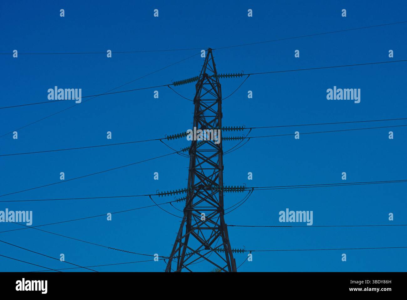 A tall steel high-voltage transmission tower stands against a blue sky ...