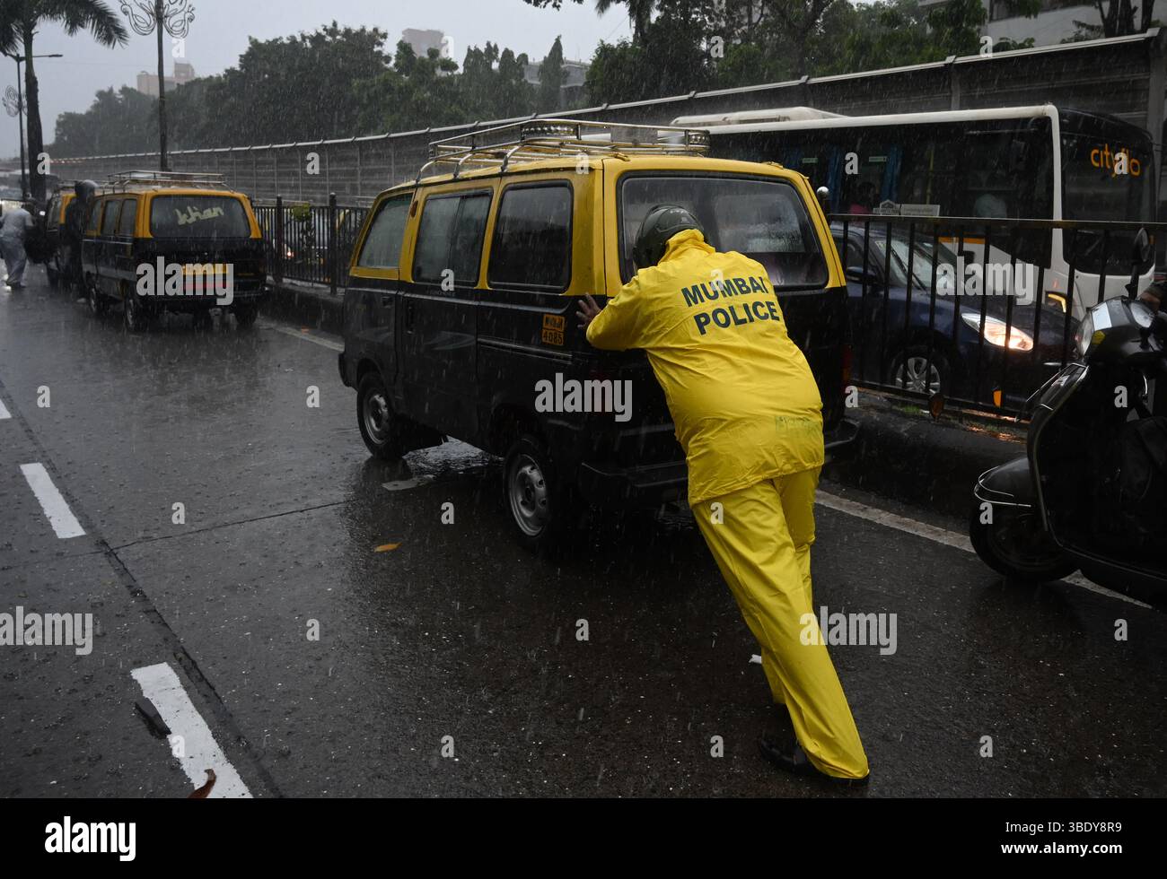 MUMBAI, INDIA - MAY 26: Mumbai policeman pushing a taxi stuck during rain at Gandhi Market in ...