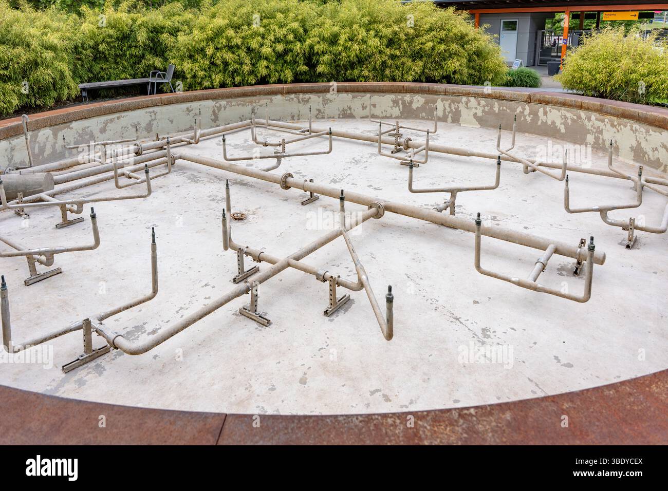 An empty fountain with a complex pipe system can be seen in the center ...