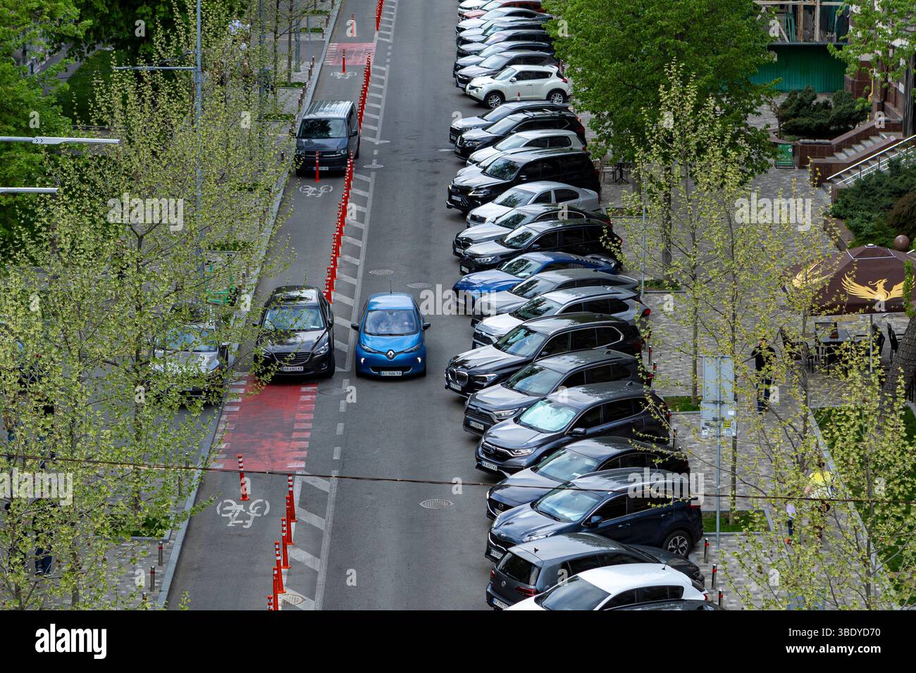 Closely parked cars line a busy city road, bordered by a carriageway ...