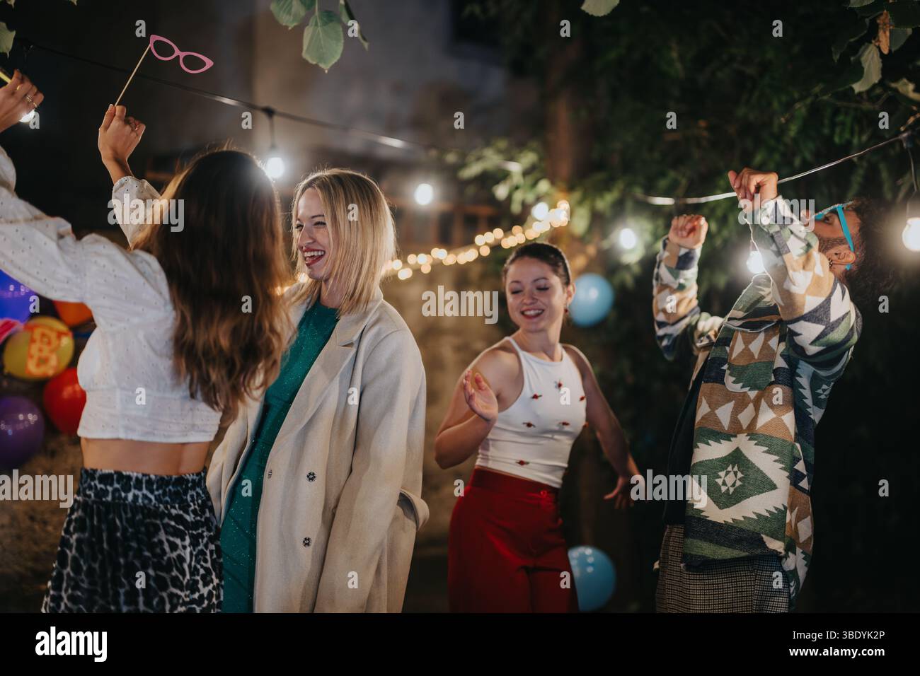 Group of friends dancing at an outdoor celebration under string lights ...