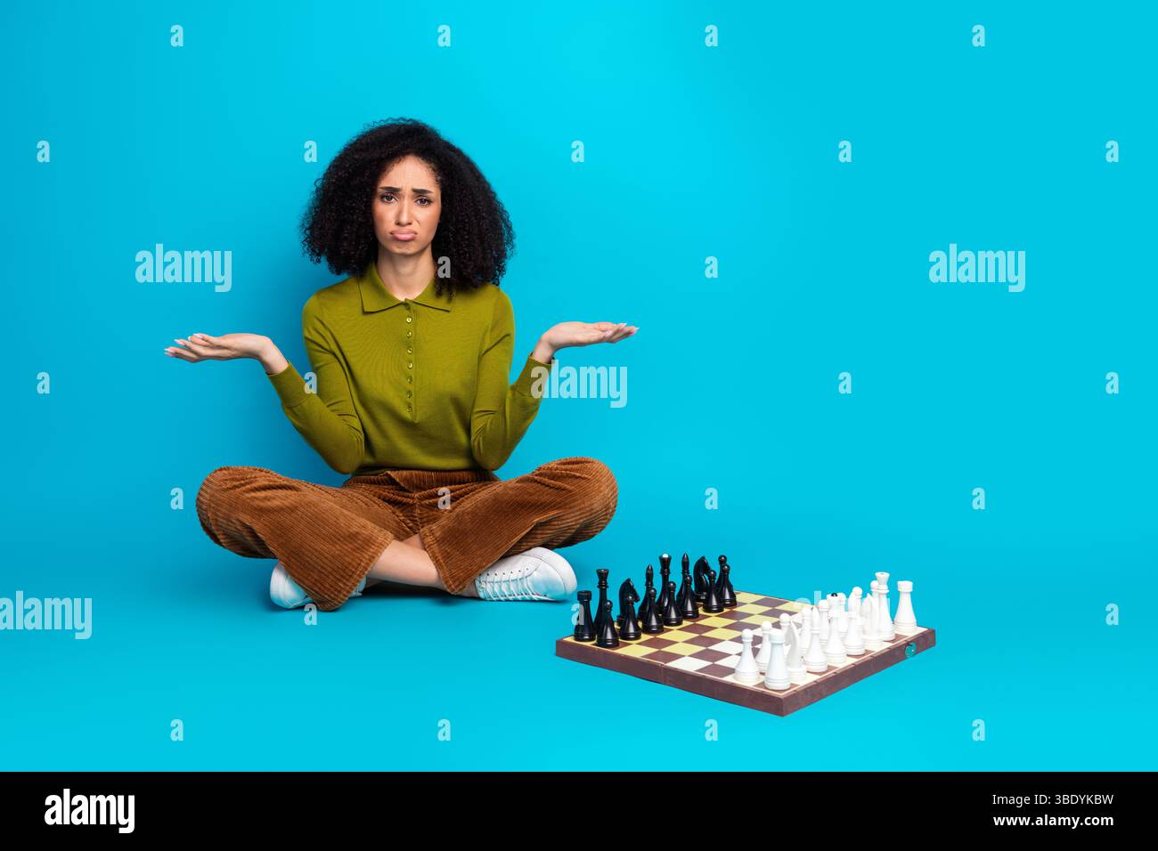 Young woman sitting on floor looking confused beside chessboard ...