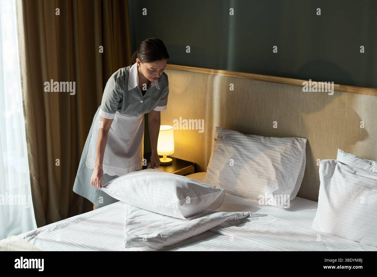 Hotel staff member making bed, carefully arranging pillows and linens ...