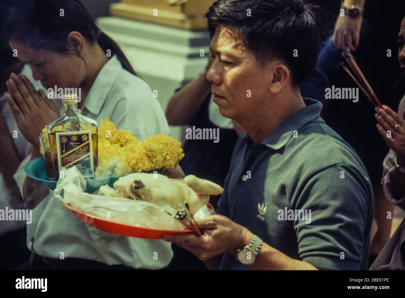 Thai man making offering of roasted chicken and Sang Thip Thai liquor ...
