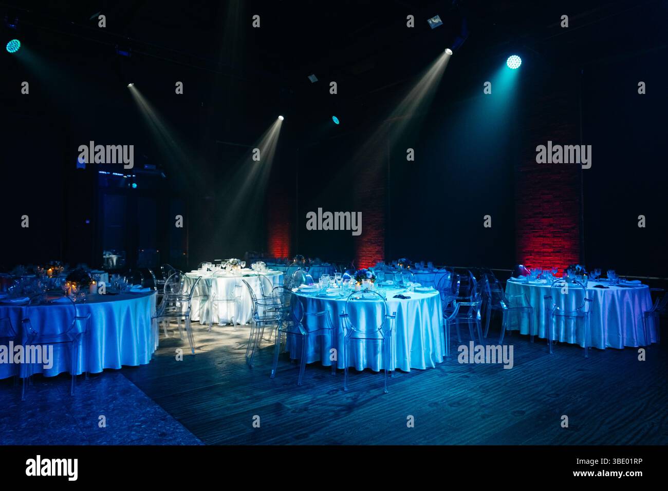 Dimly lit banquet hall with round tables covered in white linens ...