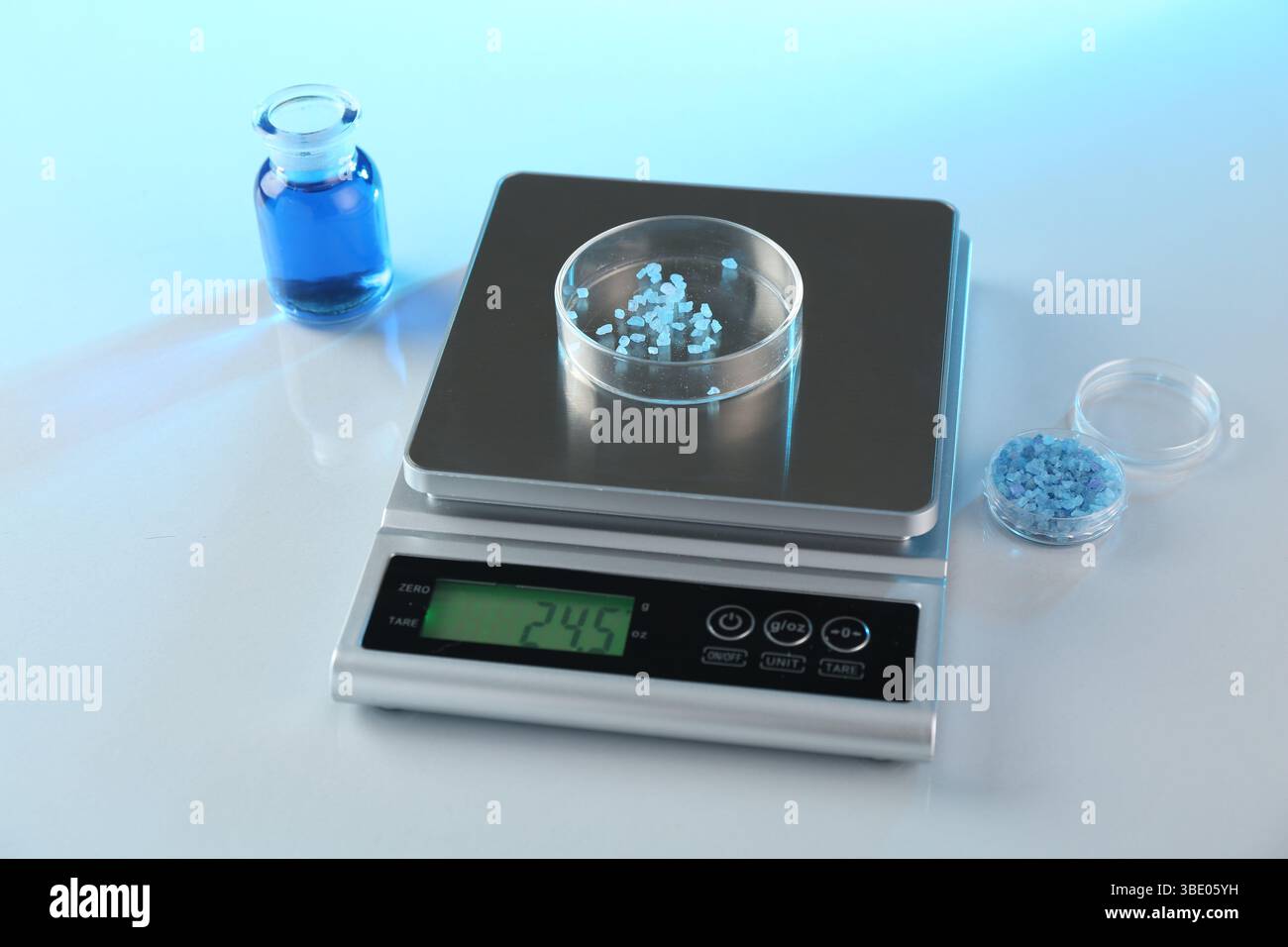 Scale with Petri dish of sample and other laboratory glassware on white ...